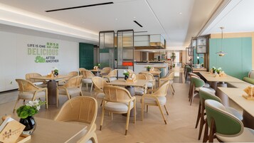 Espaço de refeições de um hotel moderno, com cadeiras de vime, mesas de madeira e parede revestida de azulejos verdes.