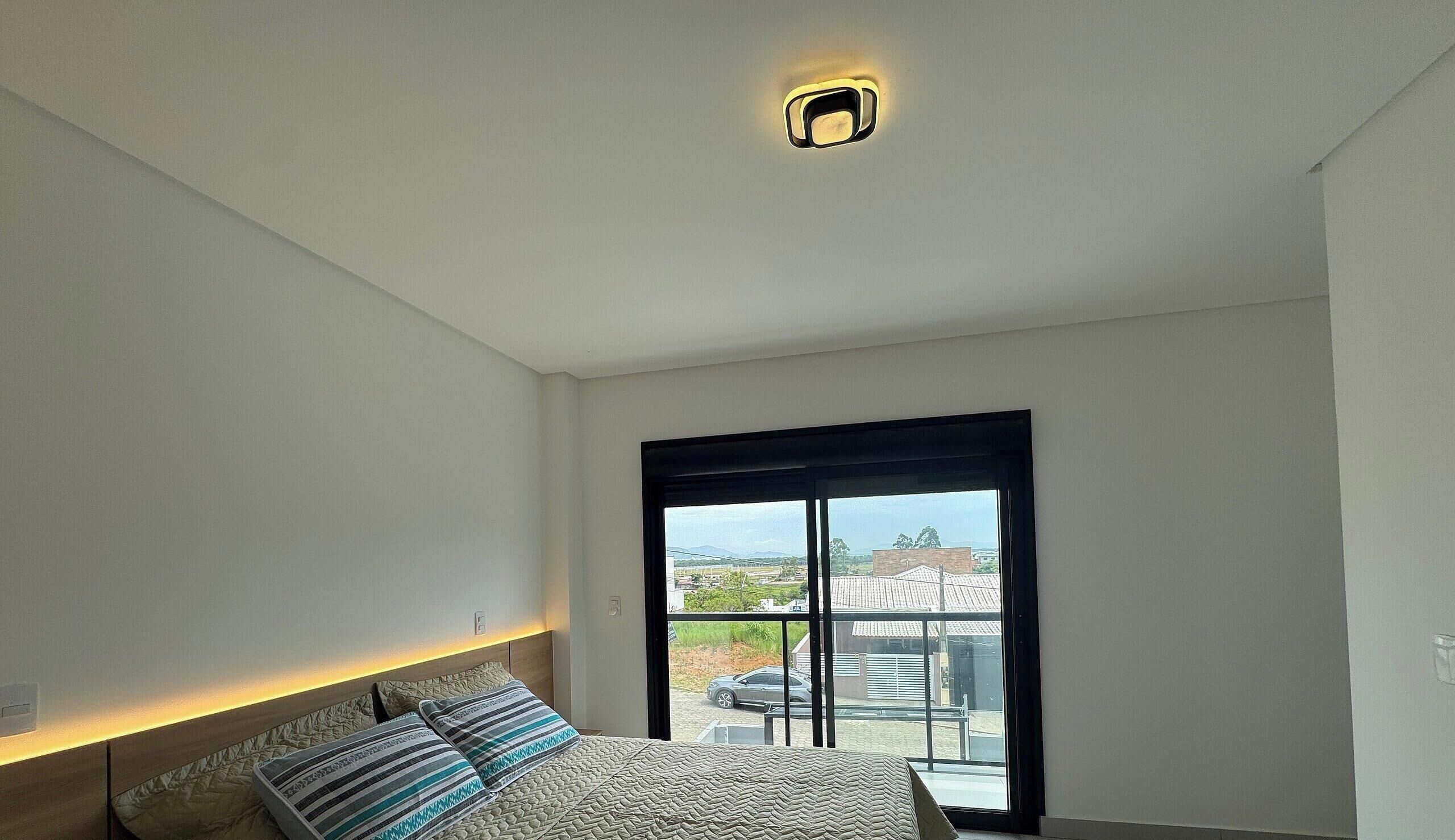 Quarto com cama, janela e luminária no teto.