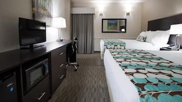 Quarto de hotel com uma cama, uma escrivaninha com televisão, uma cadeira, abajur e janela com cortinas.