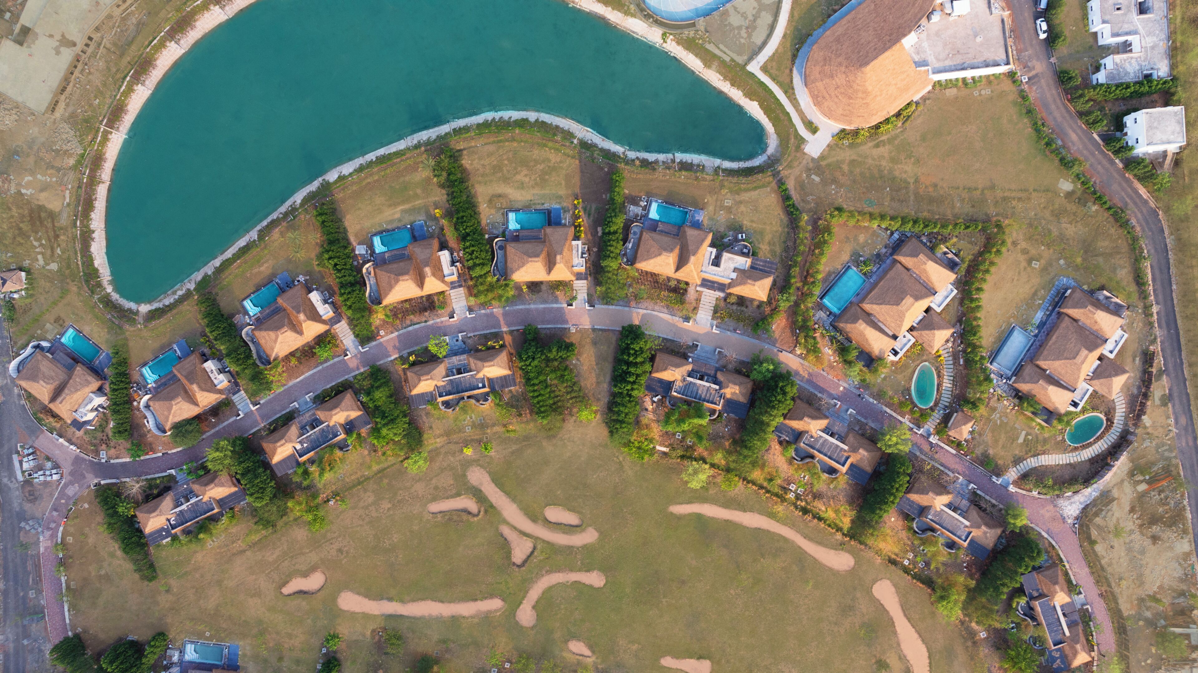 Vista aérea de um bairro residencial com casas, piscinas e uma estrada sinuosa.