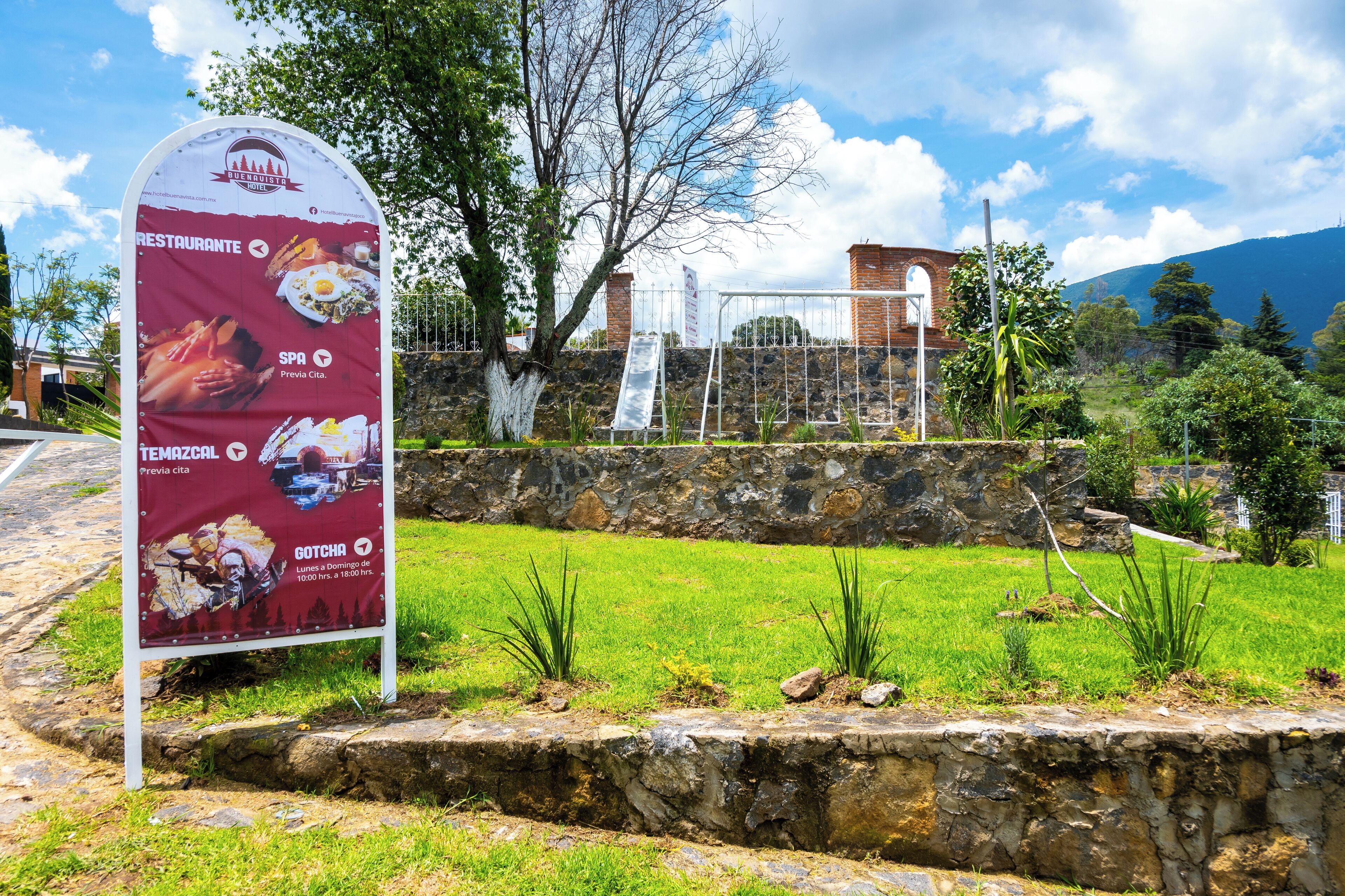 Placa publicitária de um restaurante e spa, com parede de pedra e vegetação ao fundo.
