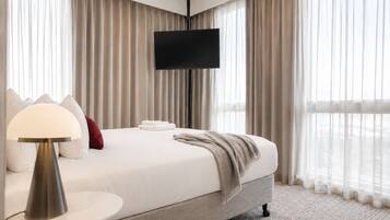 Quarto de hotel com cama, televisão de tela plana, luminária e vista para o exterior.