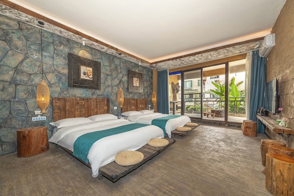 Quarto de hotel com parede de pedra, duas camas com roupa de cama branca, piso de madeira e vista para o exterior através de uma porta de vidro.