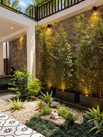 Área externa moderna com parede de pedra, plantas em vasos e espaço de estar com uma pessoa trabalhando em um laptop.