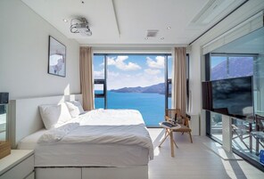 Quarto moderno com uma cama grande, uma TV e vista para o mar.