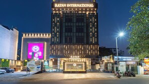 Um hotel chamado Ratan International, com uma placa chamativa, entrada bem iluminada e área de estacionamento visível.