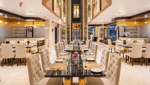 Uma sala de jantar de hotel com uma longa mesa central, diversos arranjos de assentos e um design de interiores moderno.