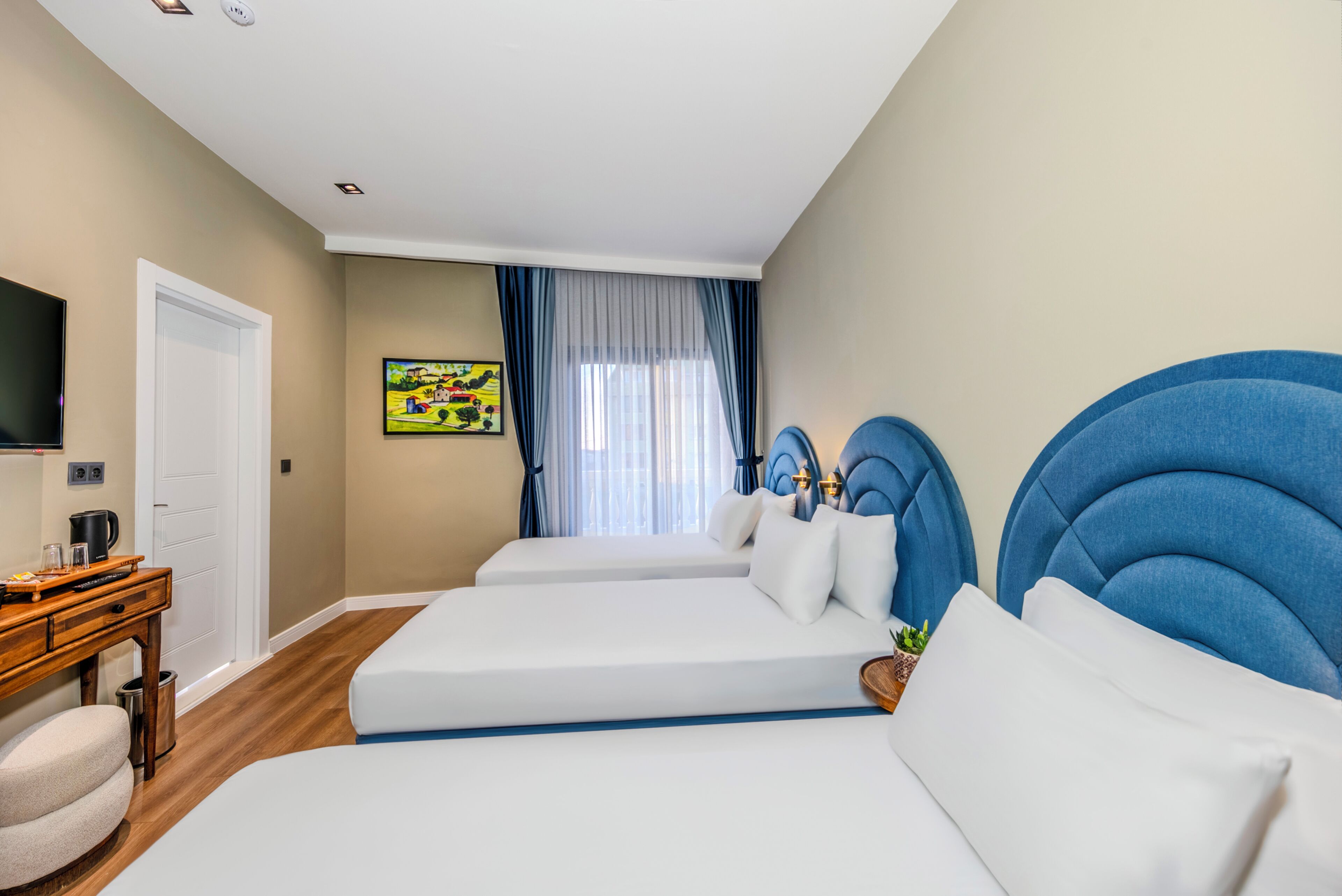 Quarto de hotel com duas camas, uma mesa com cafeteira, televisão e janela com cortinas.