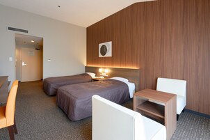 Quarto de hotel com duas camas, uma escrivaninha, uma cadeira, uma mesinha e um ar condicionado fixado na parede.