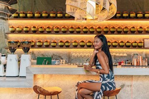Uma área de bar com uma mulher sentada, um balcão com diversos objetos e prateleiras com potes.