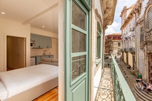 Quarto com cama, cozinha compacta e vista para uma rua estreita com edifícios.