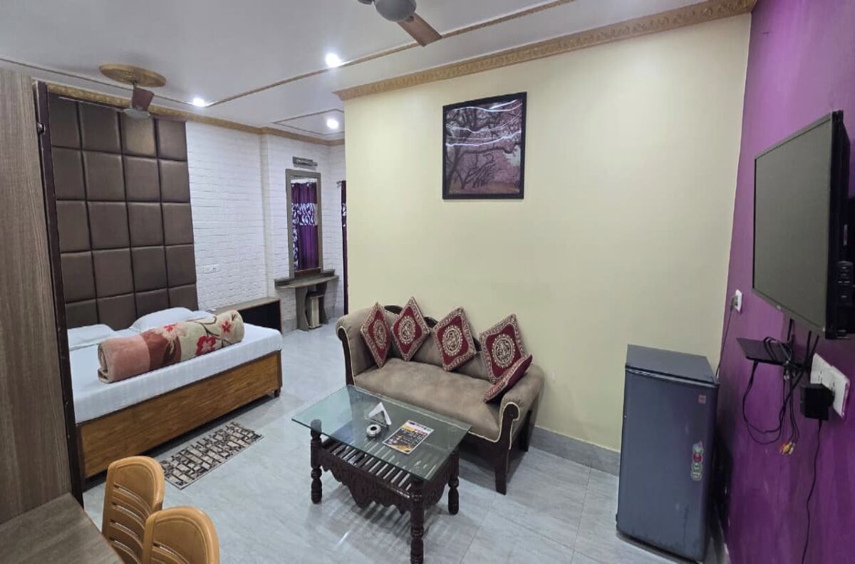 Quarto com cama, sofá, mesa de centro, televisão e pequeno frigorífico.
