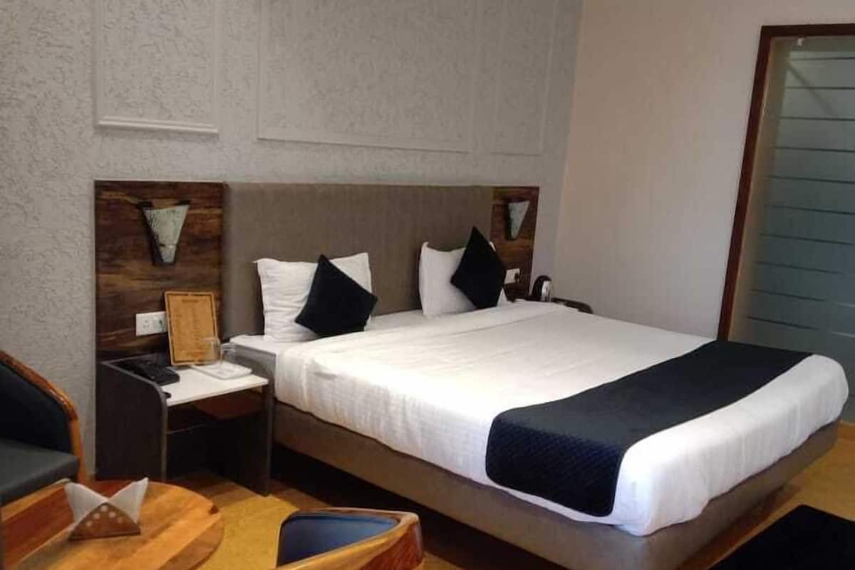 Quarto de hotel com uma cama grande, uma escrivaninha, uma cadeira e uma mesinha com uma caixa de lenços.