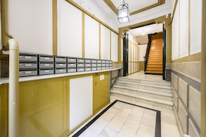 Um corredor com escadas que levam a um patamar. Há armários de armazenamento ao longo da parede e uma fileira de caixas de correio.