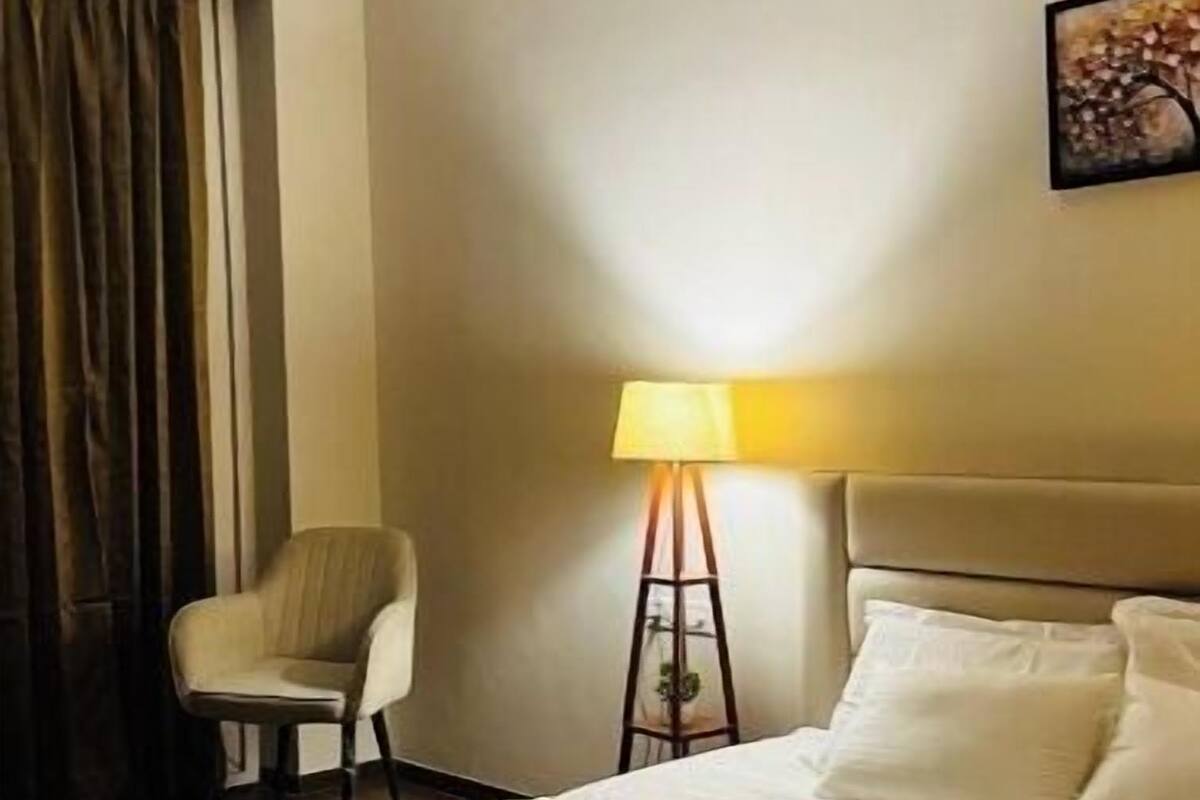 Quarto de hotel com uma cama, uma cadeira, uma luminária e um ventilador de teto.