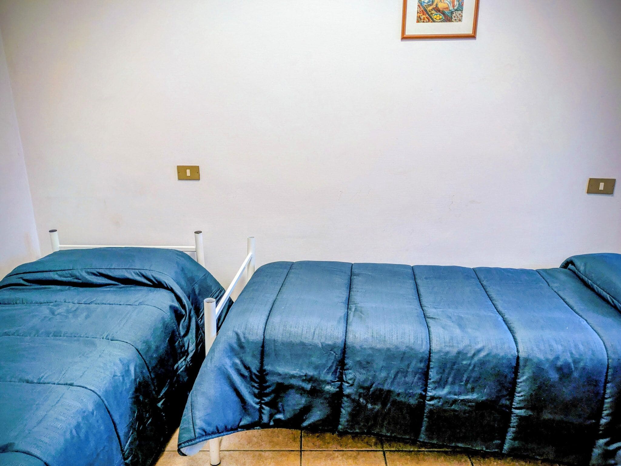Quarto com duas camas de solteiro, cada uma com colchão azul e estrutura de metal branco.