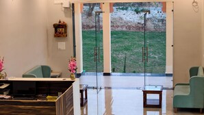 Uma área de recepção moderna com balcão, cadeiras, um vaso de flores e uma grande janela com vista para uma área gramada e um muro de pedra.