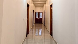 Um corredor comprido e estreito com piso polido, paredes brancas e portas de madeira em cada extremidade.