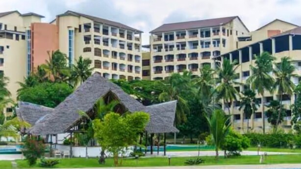 Área de piscina em resort com espreguiçadeiras e uma estrutura com telhado de palha.