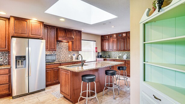 Uma cozinha com armários de madeira, uma geladeira de aço inoxidável, backsplash revestido de azulejos e um armário de vidro verde.