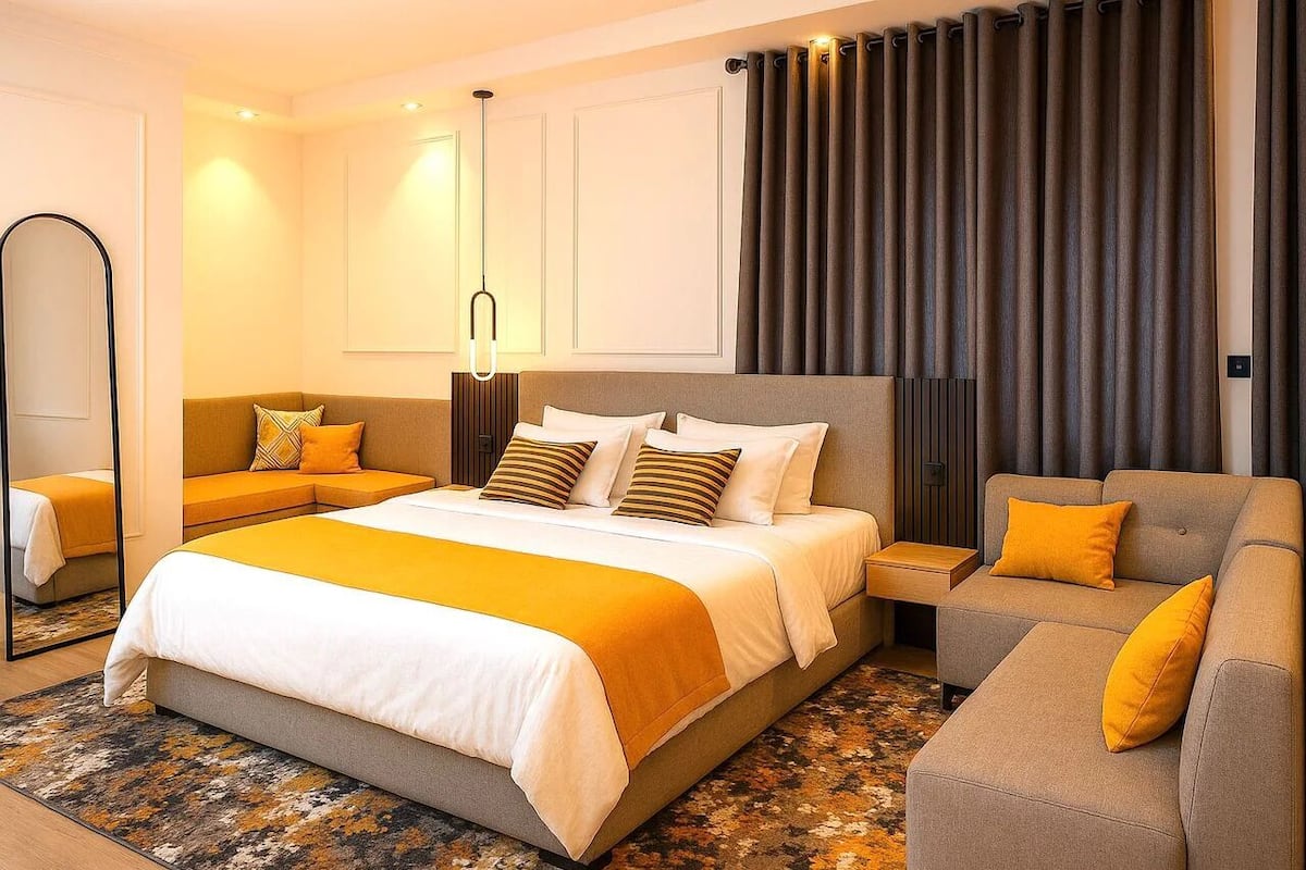 Quarto de hotel moderno com uma cama grande, um sofá, uma pequena mesa e um espelho.