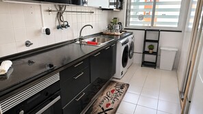 Cozinha compacta com máquina de lavar, pia e janela com vista para edifícios.