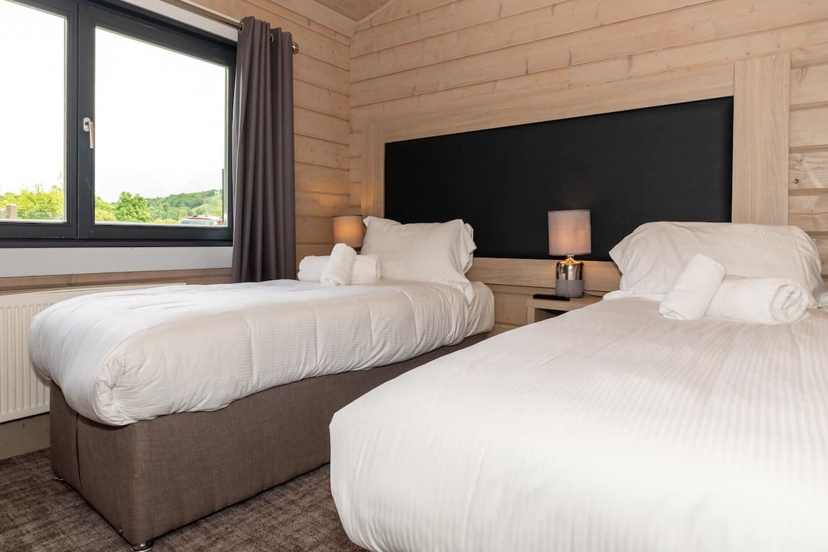 Quarto de hotel com duas camas, uma janela grande e uma lousa na parede.
