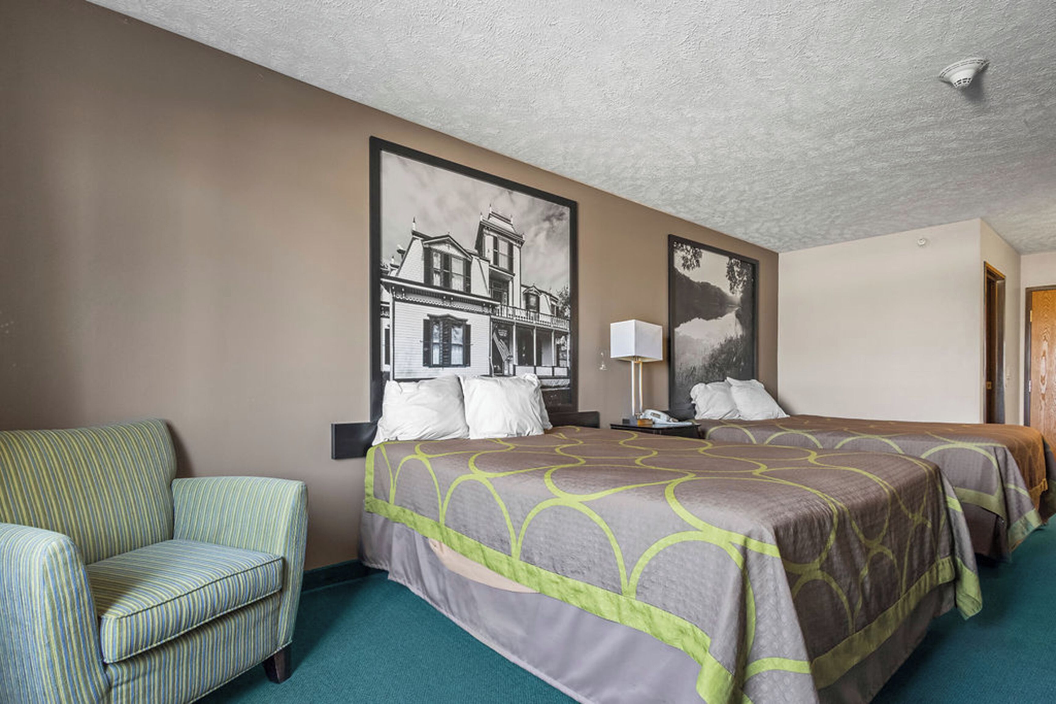Quarto de hotel com uma cama grande, uma cadeira e duas fotos emolduradas na parede.