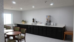 Cozinha moderna com bancada branca, armários pretos, cafeteira e um vaso com planta.