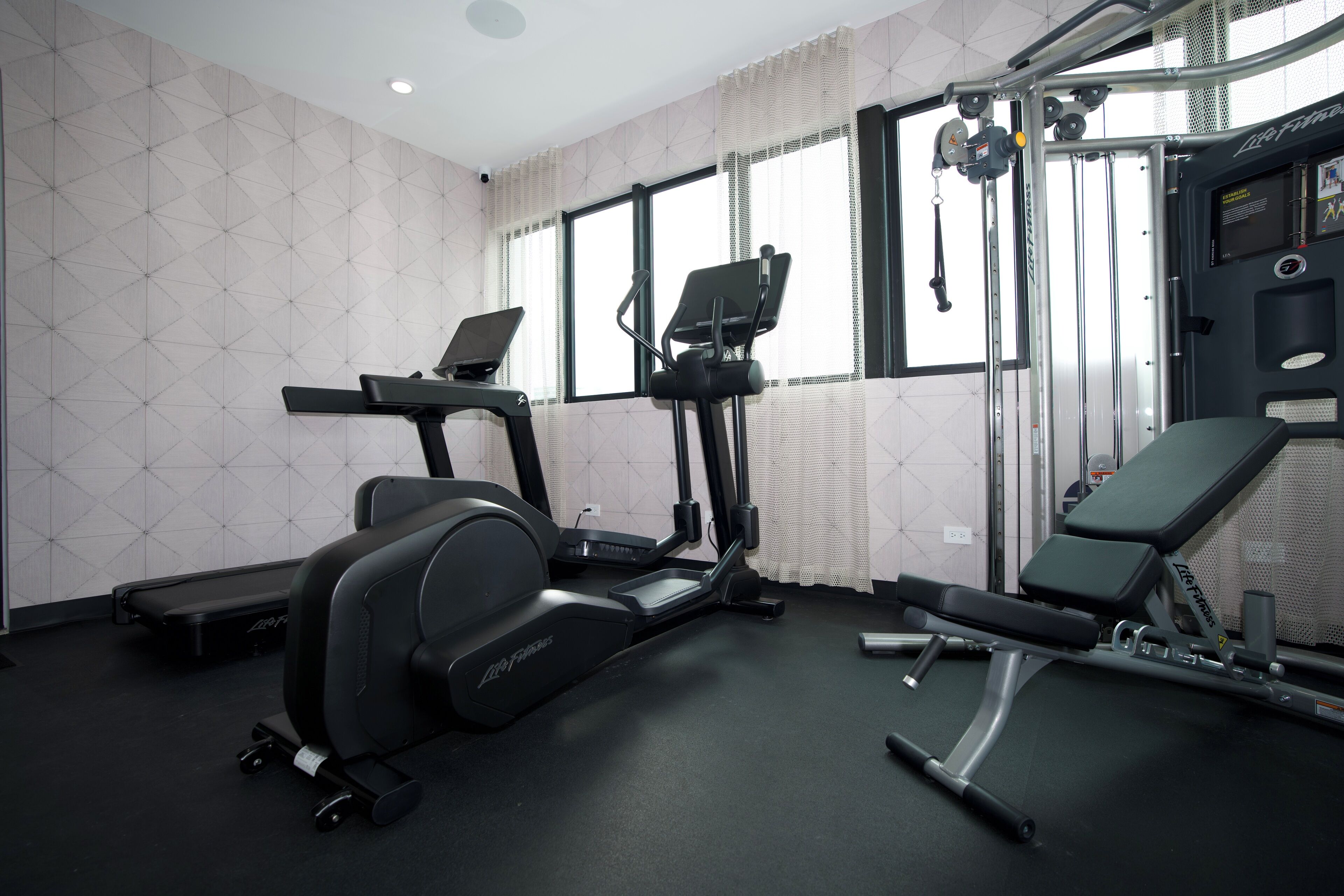 Uma academia com aparelhos de cardio, equipamentos de musculação e um banco.