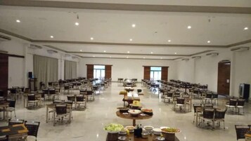 Uma sala de conferências ampla, com fileiras de cadeiras e uma mesa central repleta de comida e bebida.