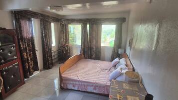 Quarto com cama, cortinas, ventilador, escrivaninha e cadeira.