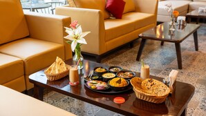 Uma área de refeições com uma mesa posta com diversos pratos, um vaso de flores e um sofá ao fundo.