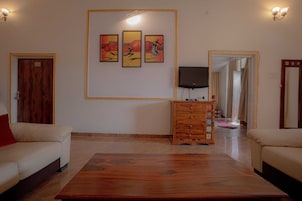 Uma sala de estar com dois sofás, uma mesa de centro de madeira, uma televisão e três obras de arte emolduradas na parede.