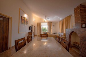 Uma sala de jantar espaçosa com uma mesa comprida, cadeiras, uma televisão e uma lareira de tijolos.