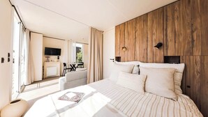 Quarto moderno com cama grande, painel de parede de madeira, televisão e vista para área externa.