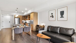 Uma sala de estar moderna com sofá de couro, uma mesa de jantar com cadeiras e uma cozinha com armários de madeira e uma geladeira.