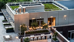 Um terraço no telhado com área de estar externa, bar e escadaria para um andar superior.