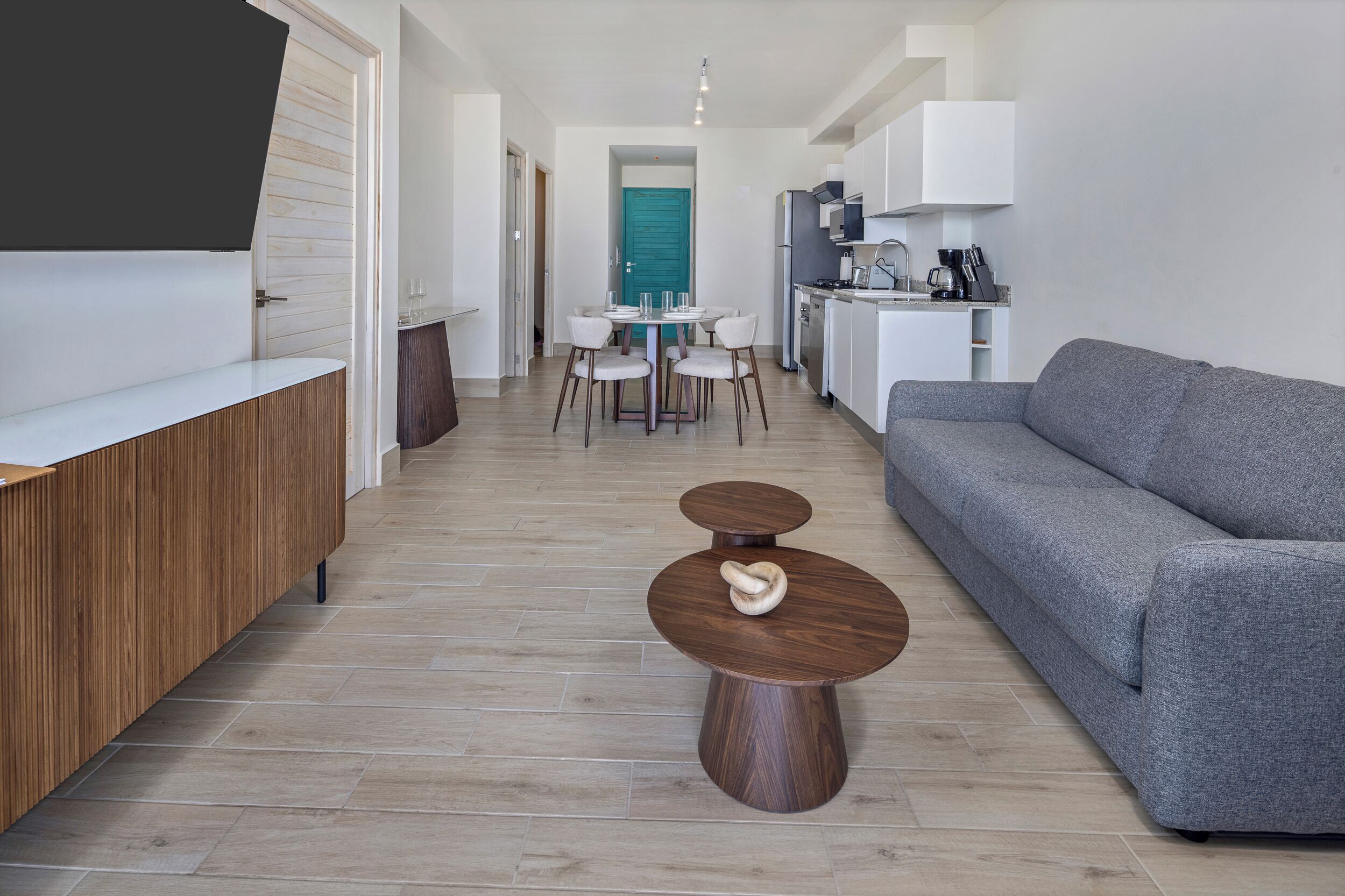 Uma sala de estar moderna com um sofá cinza, uma mesa de centro de madeira e uma área de jantar com mesa e cadeiras brancas.