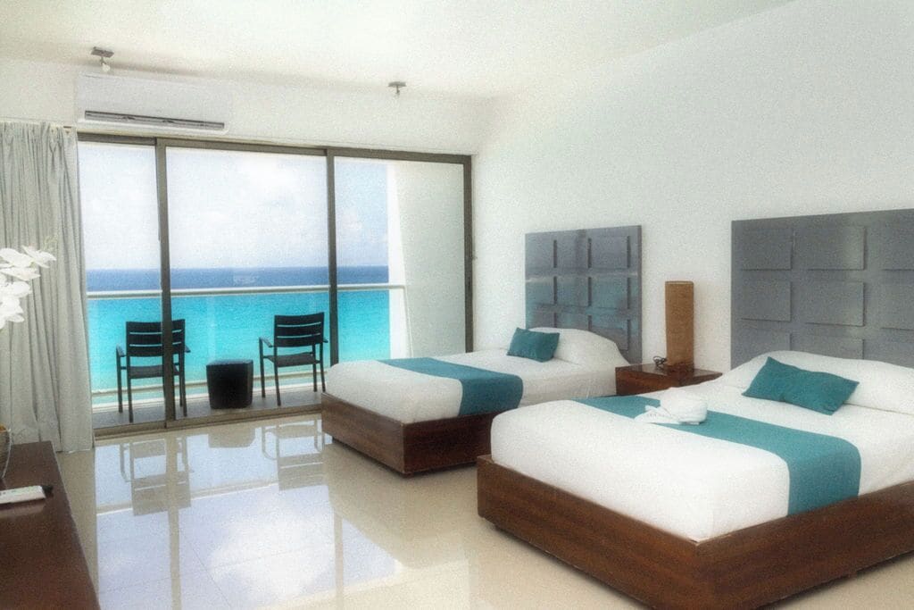Quarto de hotel com duas camas, varanda e vista para o mar, com decoração moderna.