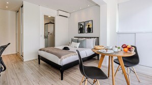 Quarto de hotel moderno com cama, mesa de jantar com cadeiras e uma pequena cozinha.