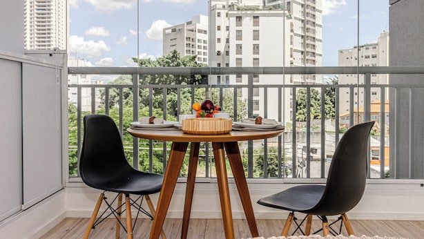 Uma varanda com uma mesa redonda, duas cadeiras pretas e uma fruteira.
