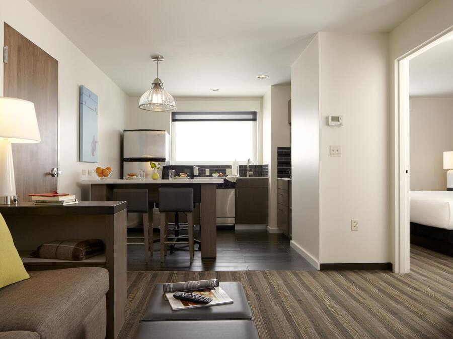 Quarto de hotel moderno com sala de estar, cozinha compacta e quarto separado.