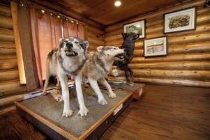 Interior de uma cabana de madeira com duas estátuas de lobo em uma plataforma.