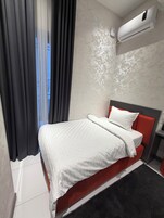 Quarto de hotel com cama, mesa de cabeceira, cabeceira vermelha, janela com cortinas e unidade de ar condicionado.