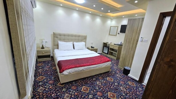 Quarto de hotel com uma cama grande, uma mesa de cabeceira, uma televisão e uma escrivaninha com cadeira.