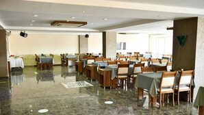 Uma sala de jantar ampla, com várias mesas e cadeiras, piso de mármore polido e cores neutras.