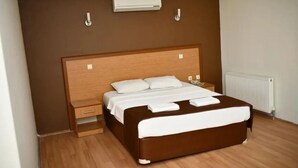 Quarto com cama de madeira, roupa de cama branca, mesa de cabeceira, gaveta e ar condicionado fixado na parede.