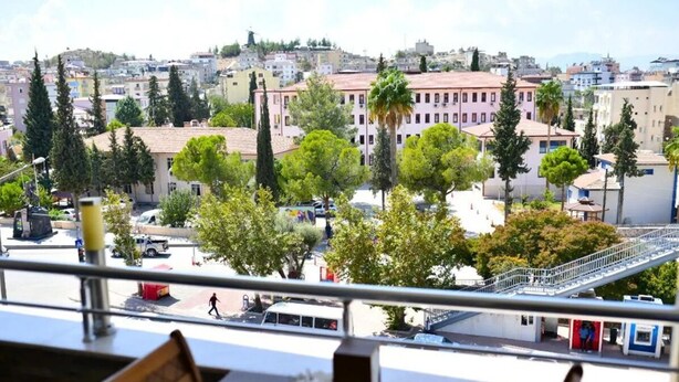 Vista de uma varanda com vista para um horizonte urbano, incluindo edifícios, árvores e uma passarela para pedestres.