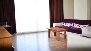 Uma sala de estar moderna com uma mesa de centro de madeira, um sofá roxo com almofadas estampadas e uma poltrona branca.